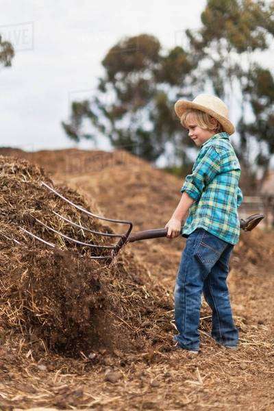 Boy using pitchfork in haystack - Royalty-free Stock Photo | Dissolve