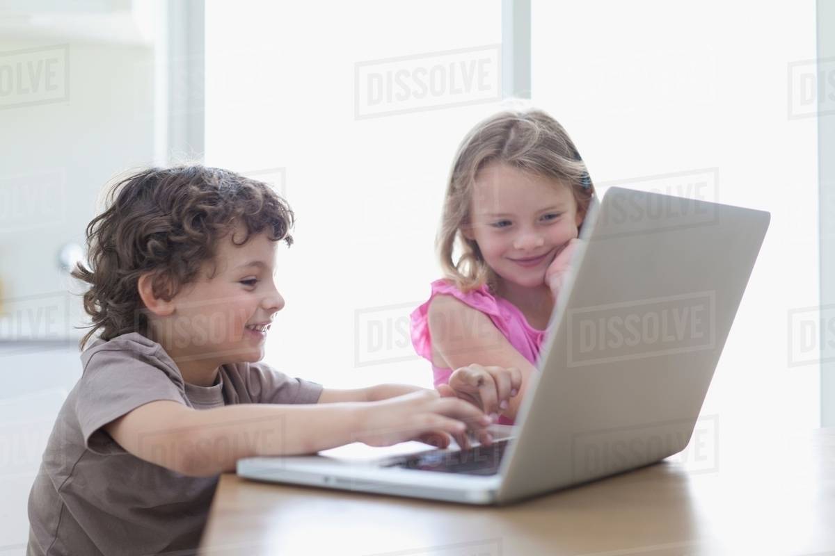 Smiling children using laptop together - Stock Photo - Dissolve