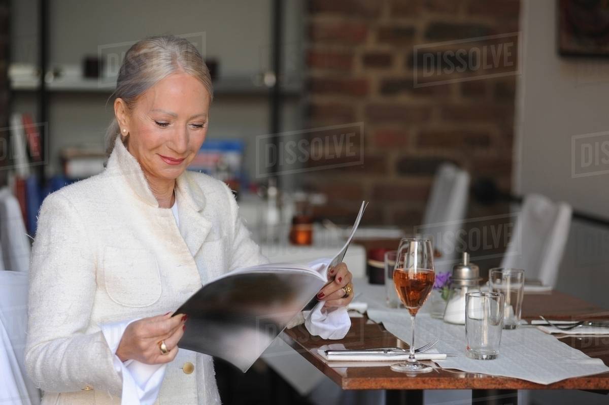 Older woman reading magazine in cafe - Stock Photo - Dissolve