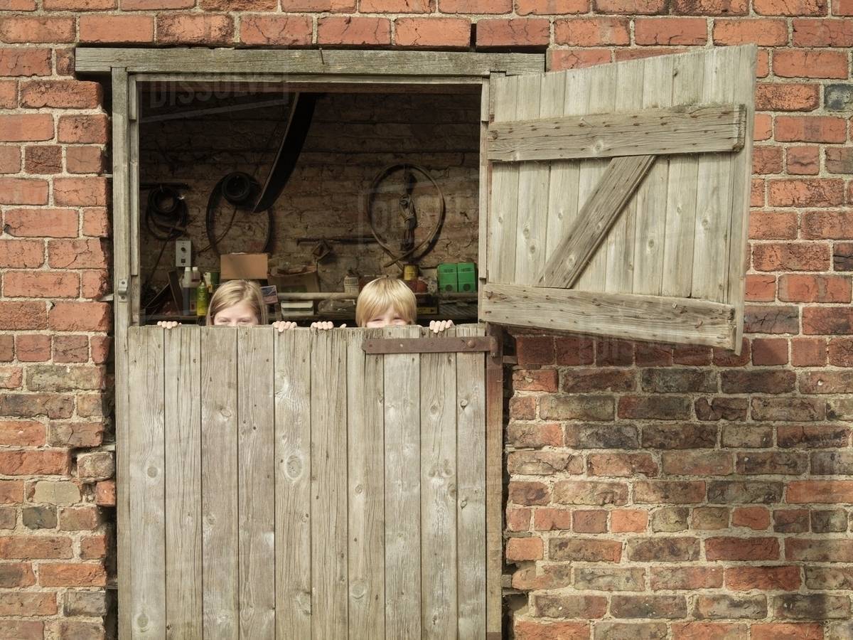 Teenage girl and brother hiding behind barn door - Stock Photo - Dissolve