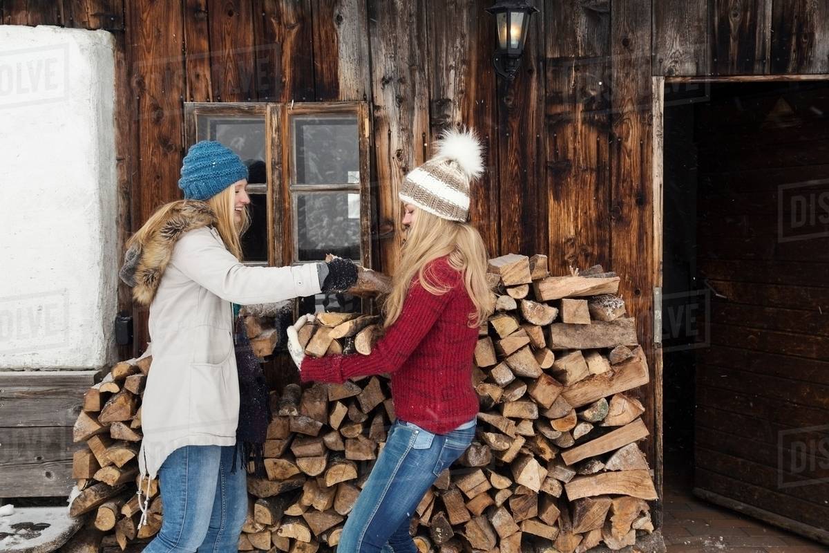 Two young female friends stacking logs outside cabin - Royalty-free ...