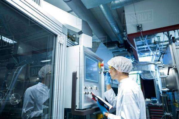 Male scientist with notebook adjusting control panel in lab cleanroom ...