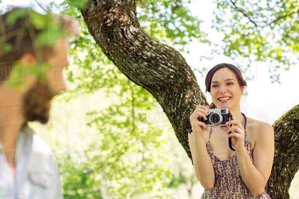 Young woman underneath tree taking photograph of young man - Royalty ...