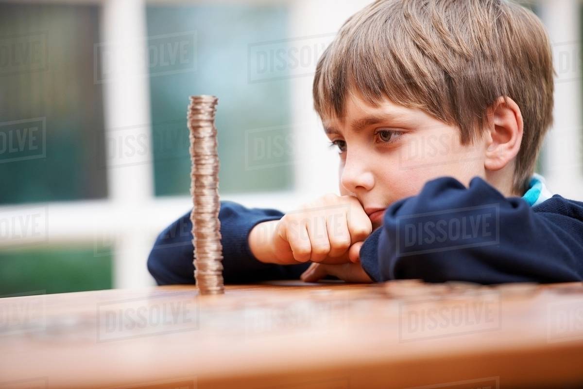 Boy looking at a tower of coins - Stock Photo - Dissolve