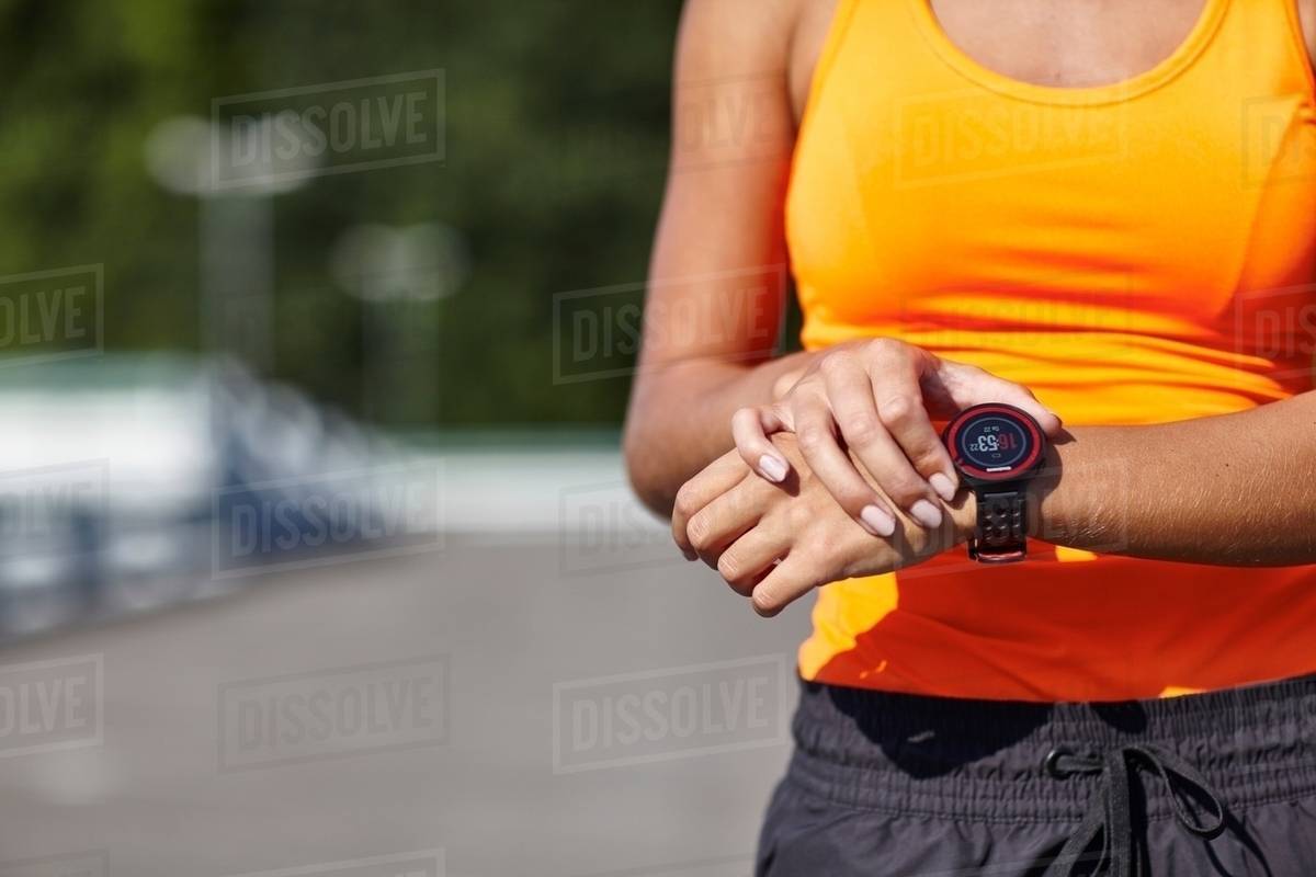 Cropped shot of young female runner setting smartwatch in parking lot ...