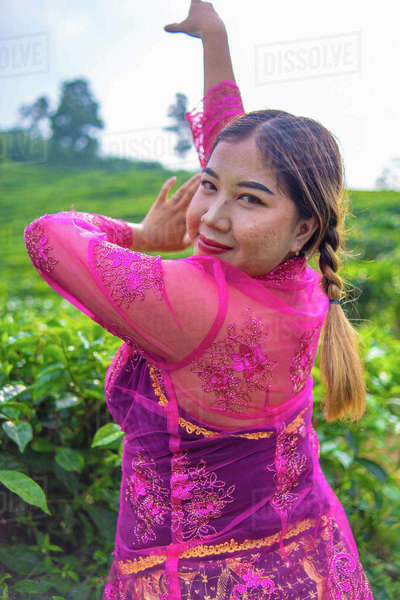 an Asian woman in a pink costume is posing in front of a tea plantation ...