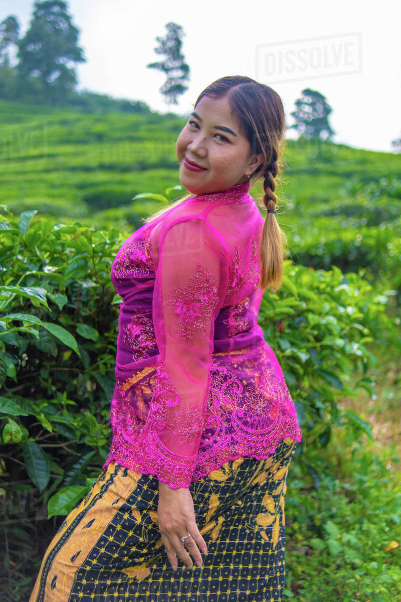 an Asian woman in a pink costume is posing in front of a tea plantation ...