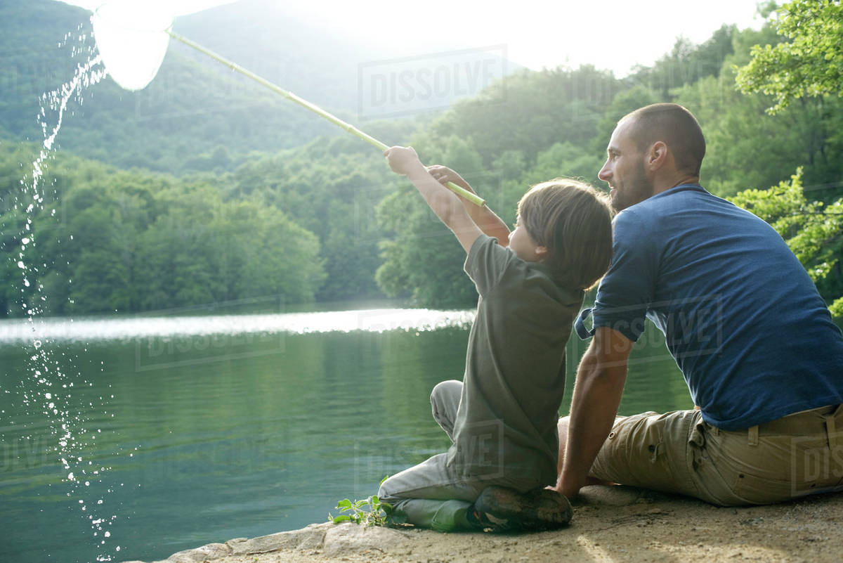 Father and son fishing, boy holding up fishing net - Stock Photo - Dissolve
