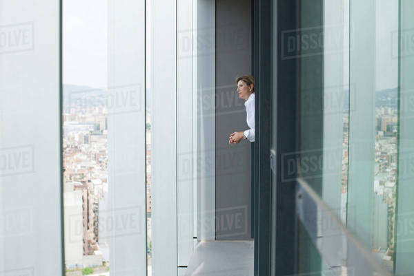 Woman looking out of office window at view of city - Stock Photo - Dissolve