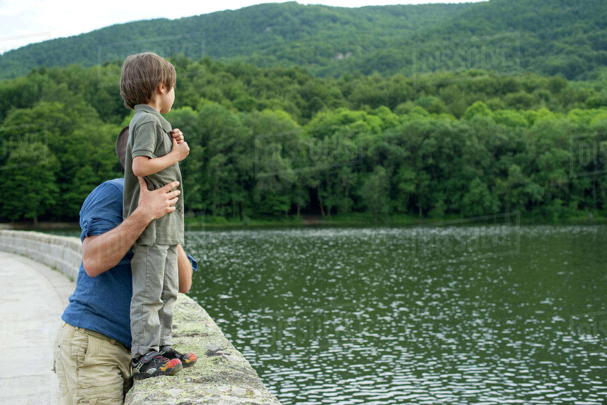 Father holding son standing on stone wall - Stock Photo - Dissolve
