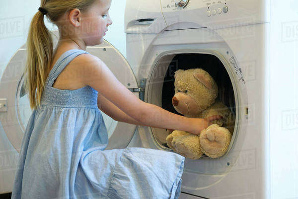 Little girl taking teddy bear out of dryer - Royalty-free Stock Photo ...