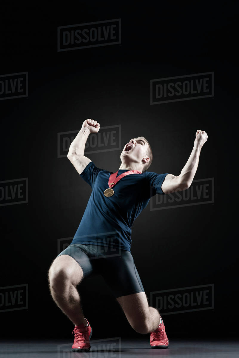 Male athlete shouting with arms raised in victory - Stock Photo - Dissolve