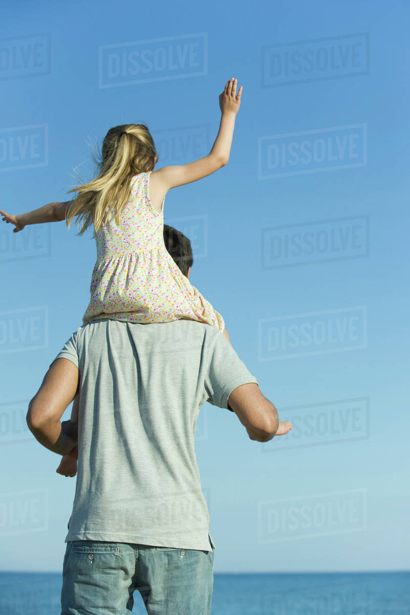 Father carrying daughter on his shoulders, rear view - Stock Photo - Dissolve