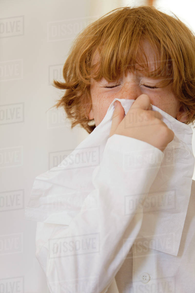 Boy blowing nose on tissue with eyes closed - Stock Photo - Dissolve
