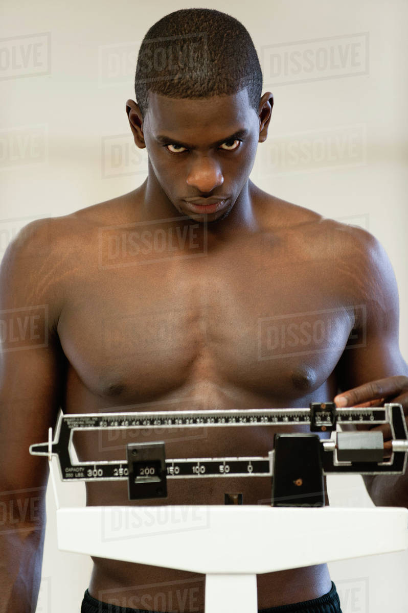 Young man standing on weight scale - Stock Photo - Dissolve