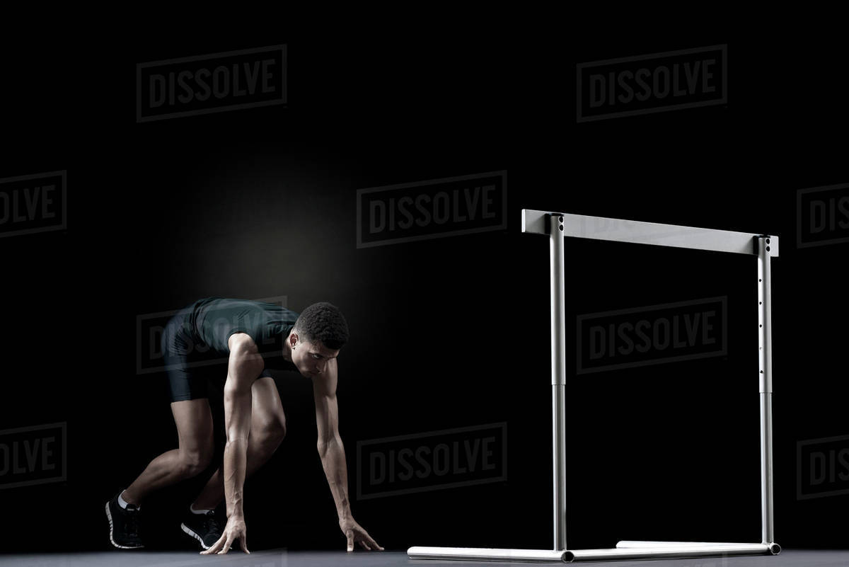 Male athlete at starting position in front of hurdle - Stock Photo ...