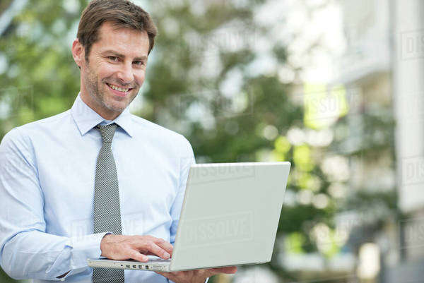 Businessman using laptop outdoors - Stock Photo - Dissolve