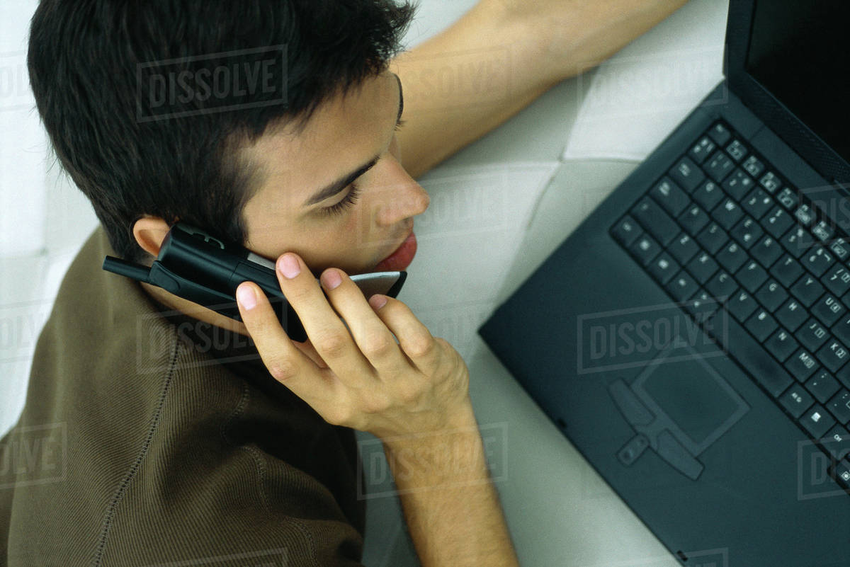 Man phoning, leaning on elbow, using laptop computer - Royalty-free ...