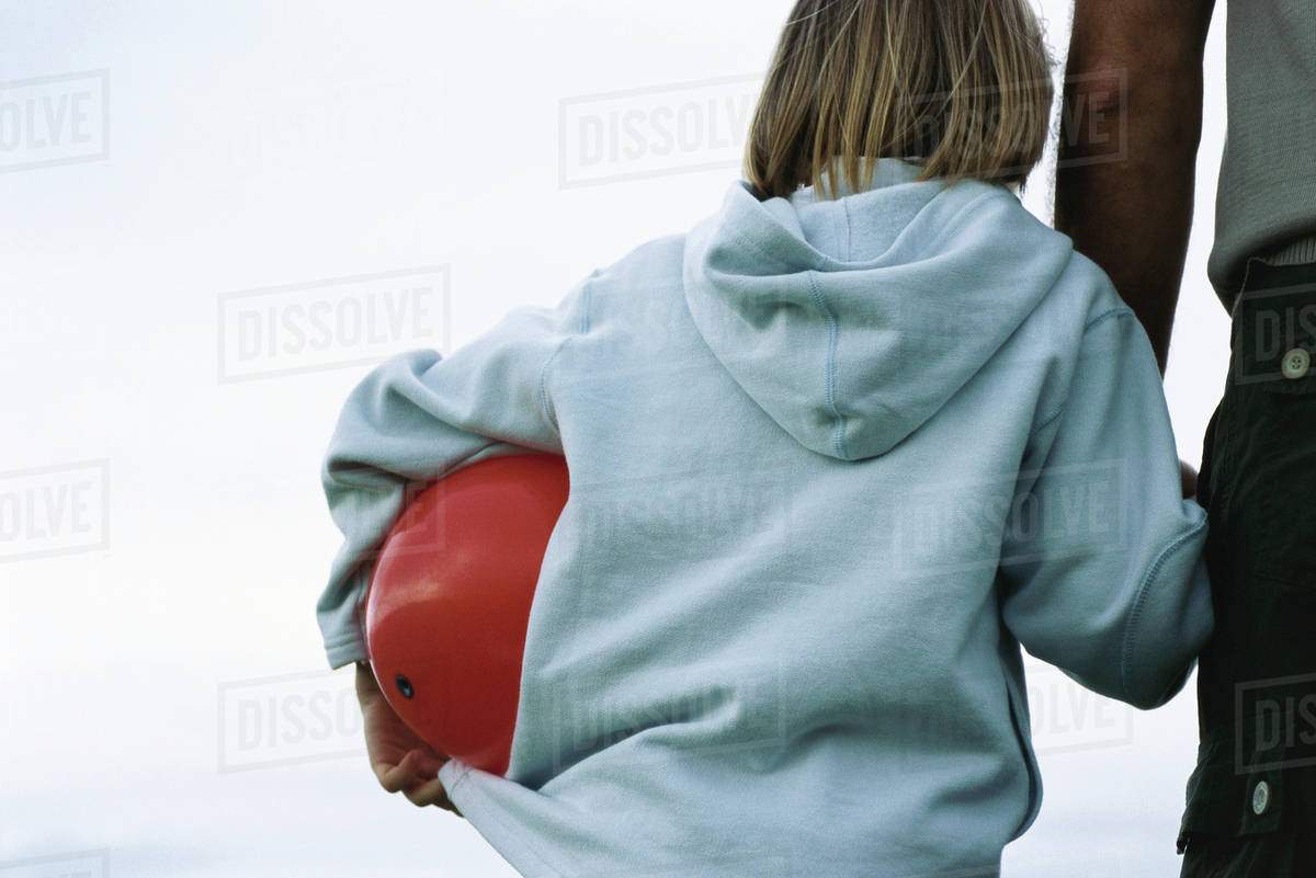 Young boy holding father's hand, carrying ball under arm, rear view ...