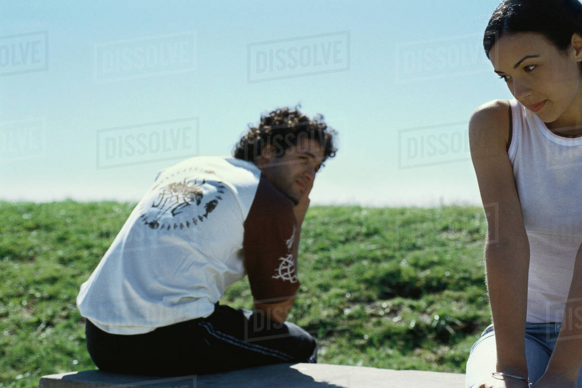 Young man and woman sitting on bench, man glancing sideways over ...