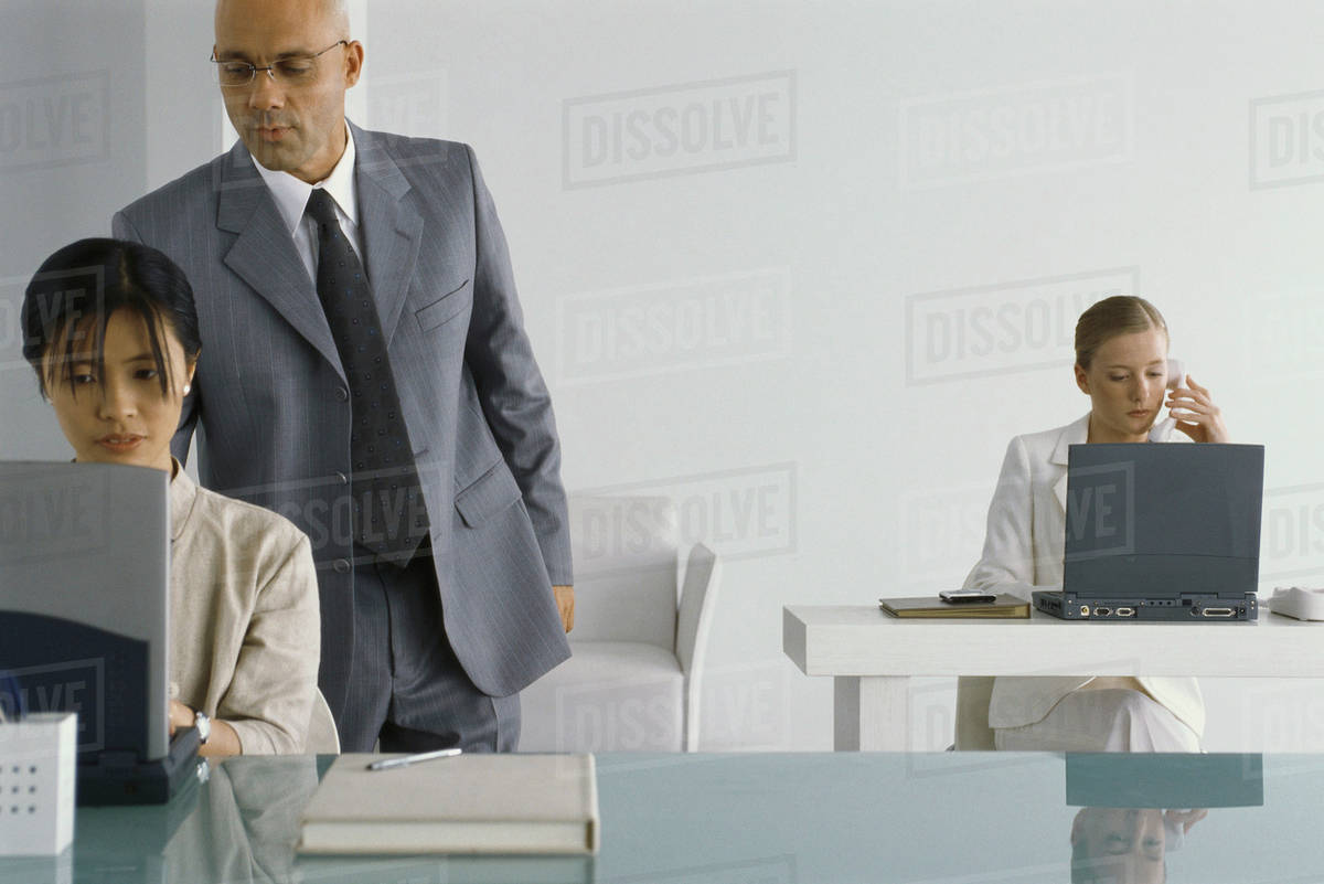 Manager standing, looking over shoulder of female employee while she ...