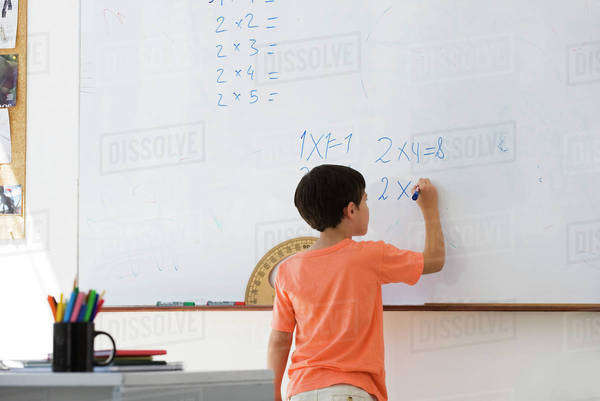 Elementary school student working math equations on whiteboard ...