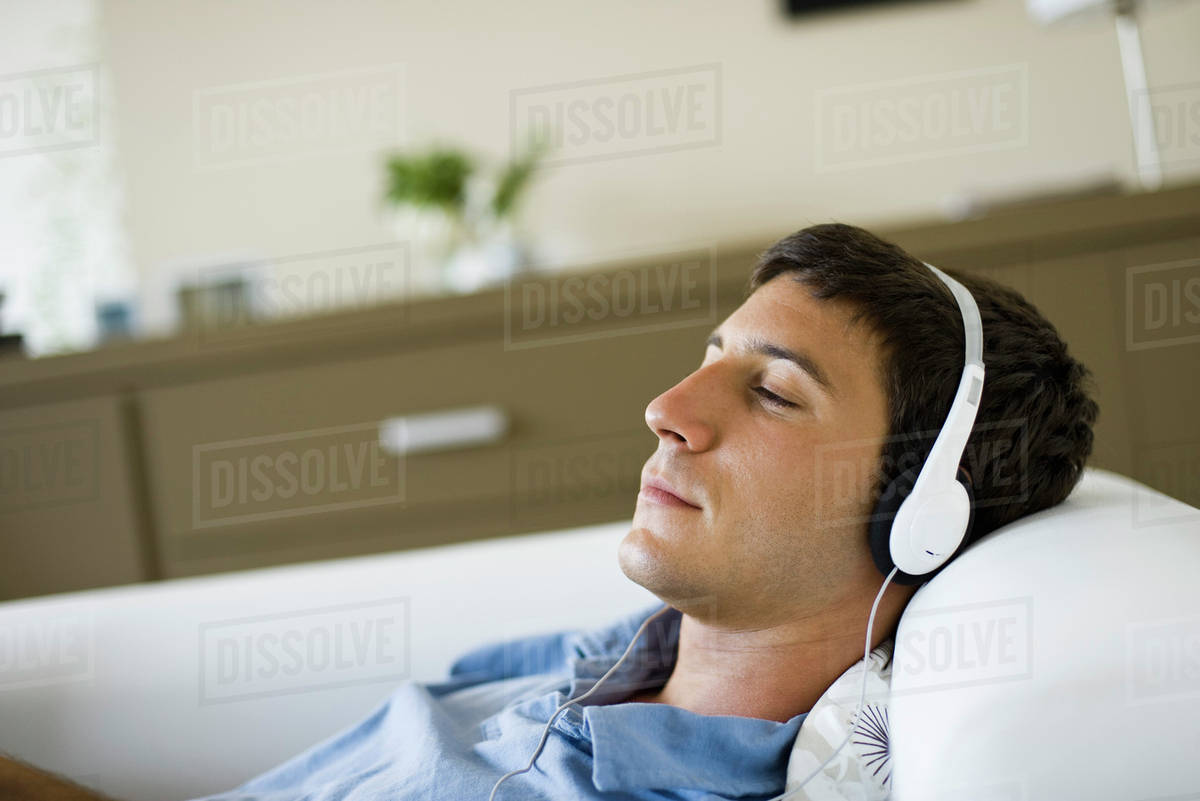 Young man relaxing on sofa listening to music with headphones - Royalty ...