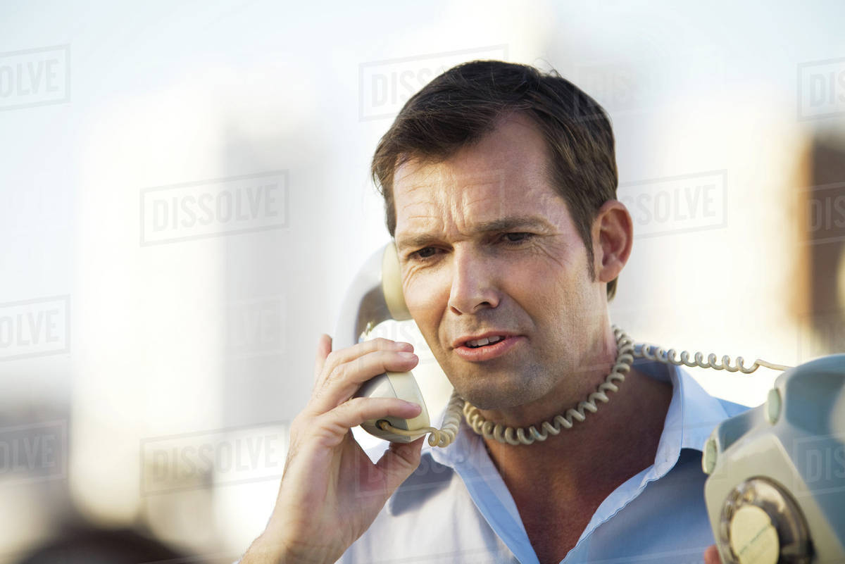 Man talking on landline phone, cord wrapped around his neck, close-up ...