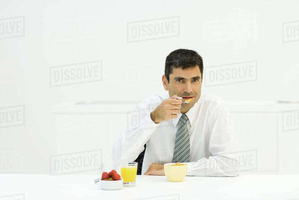 Man sitting at table, eating healthy breakfast, looking at camera ...