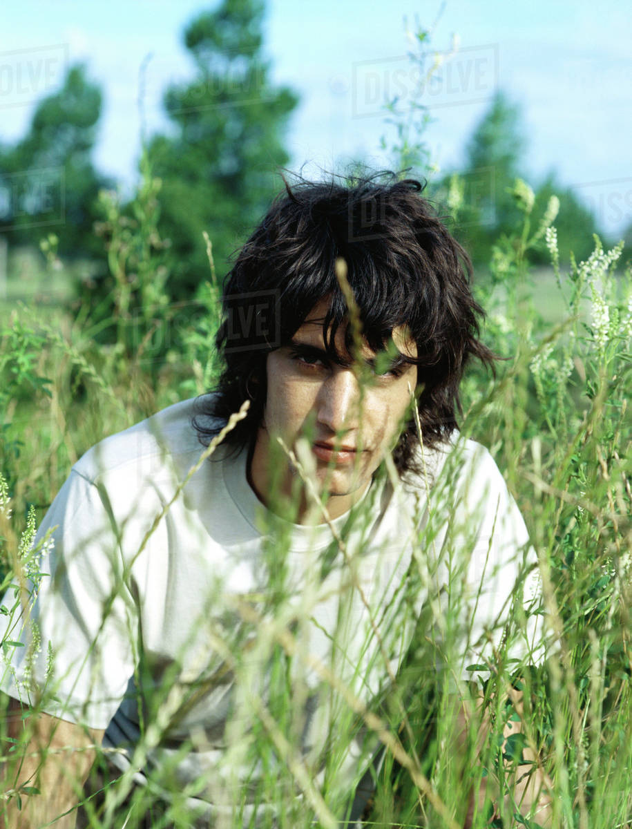 Male crouching in tall grass, looking at camera, portrait - Royalty ...