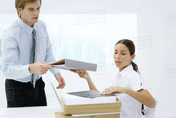 Professional woman handing binder to colleague from stack of many ...