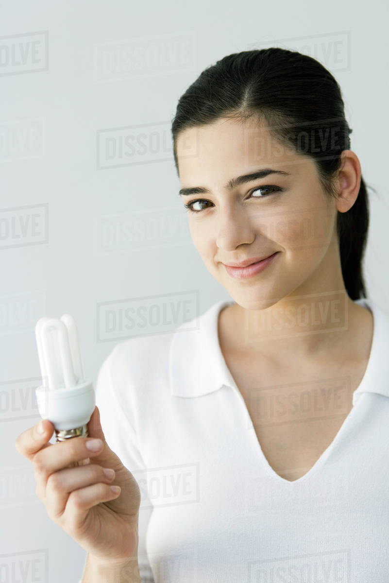 Young woman holding energy efficient light bulb, smiling at camera ...