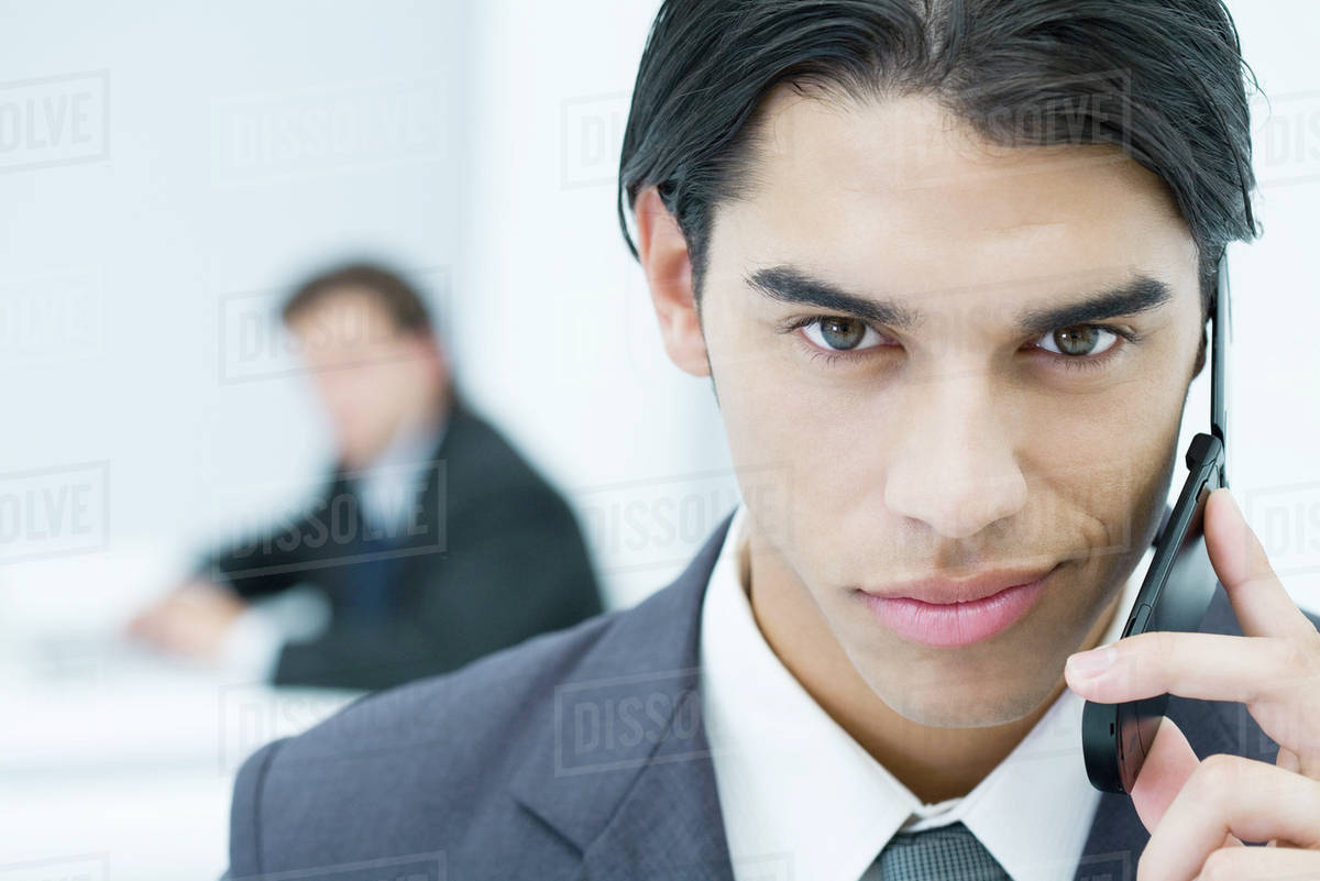 Young professional man holding cell phone, smirking at camera, portrait ...