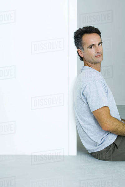 Man sitting on the ground, leaning against doorway, looking over ...