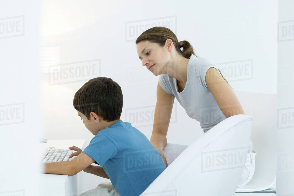 Boy typing on keyboard, mother looking over shoulder - Royalty-free ...