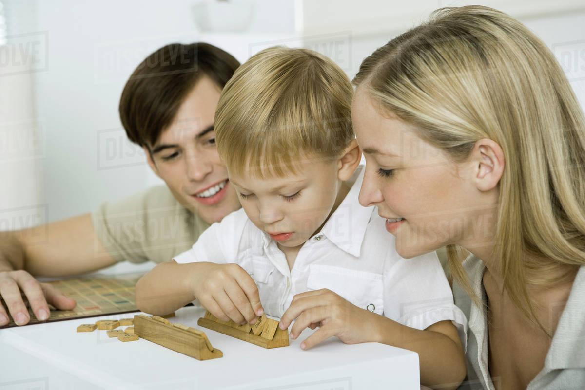 Parents watching as little boy arranges game pieces - Stock Photo ...