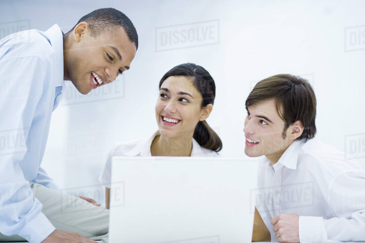 Young professionals sitting around laptop computer, leaning close ...