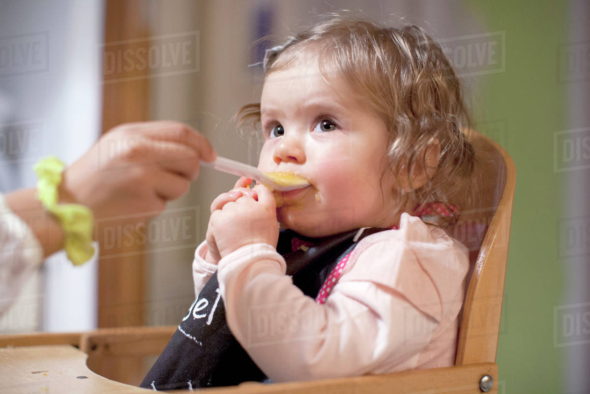 Baby girl being fed by parent, cropped - Stock Photo - Dissolve