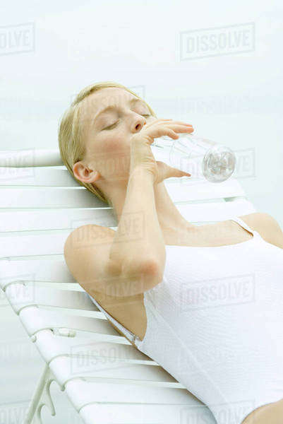Teenage girl wearing bathing suit, sitting in lounge chair, drinking ...