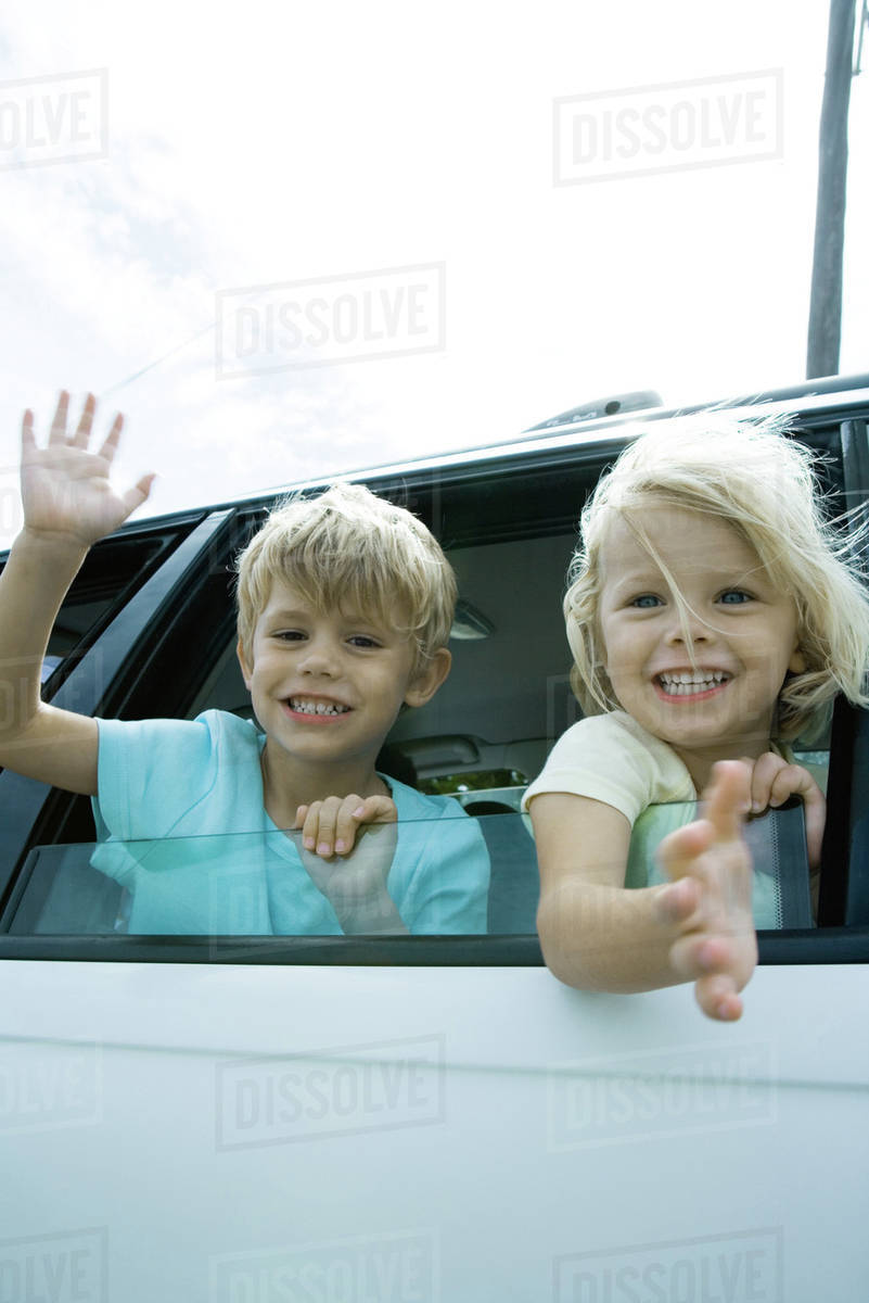 Children sticking heads out of car window, waving - Stock Photo - Dissolve
