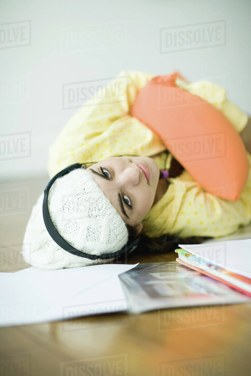 Young woman lying on floor listening to headphones, neglecting homework ...