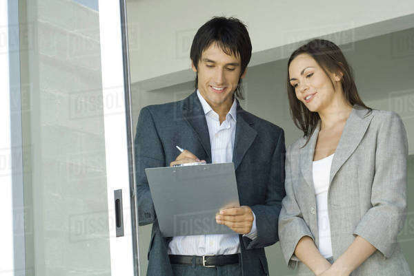 Male real estate agent showing house to female client, writing on ...