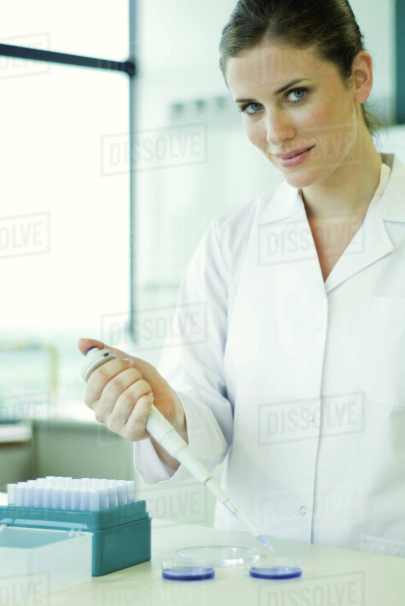 Female lab worker dropping solution into Petri dish, smiling at camera ...