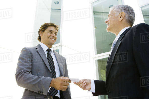 Two businessmen exchanging business card, smiling at each other, low ...