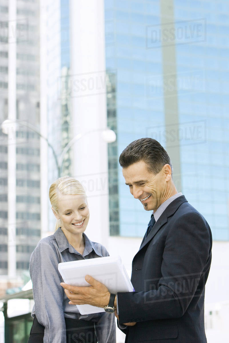 Two business associates standing outdoors, looking at file together ...