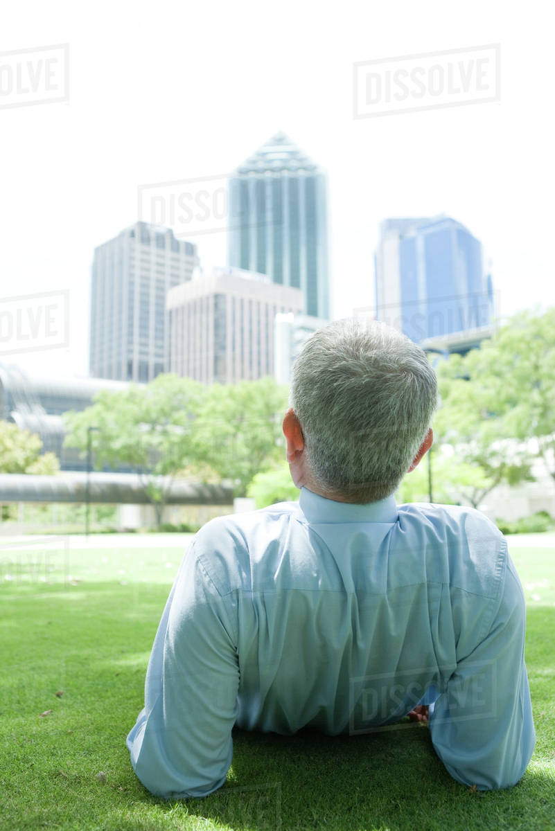 Mature man reclining on ground, looking at urban scene, rear view ...