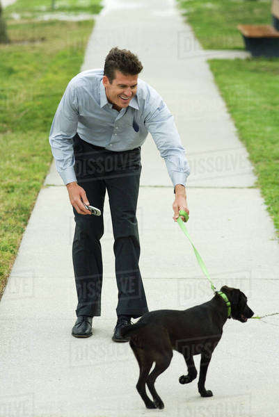 Man walking dog on sidewalk, bending forward, smiling - Royalty-free ...