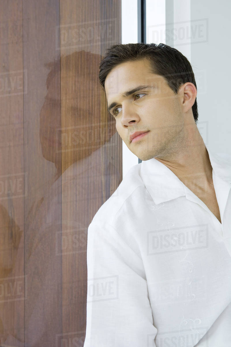 Young man leaning against window, looking out, close-up - Royalty-free ...