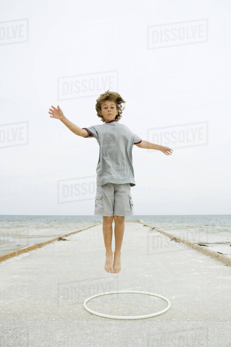 Boy jumping over plastic hoop with arms out, looking at camera - Stock ...