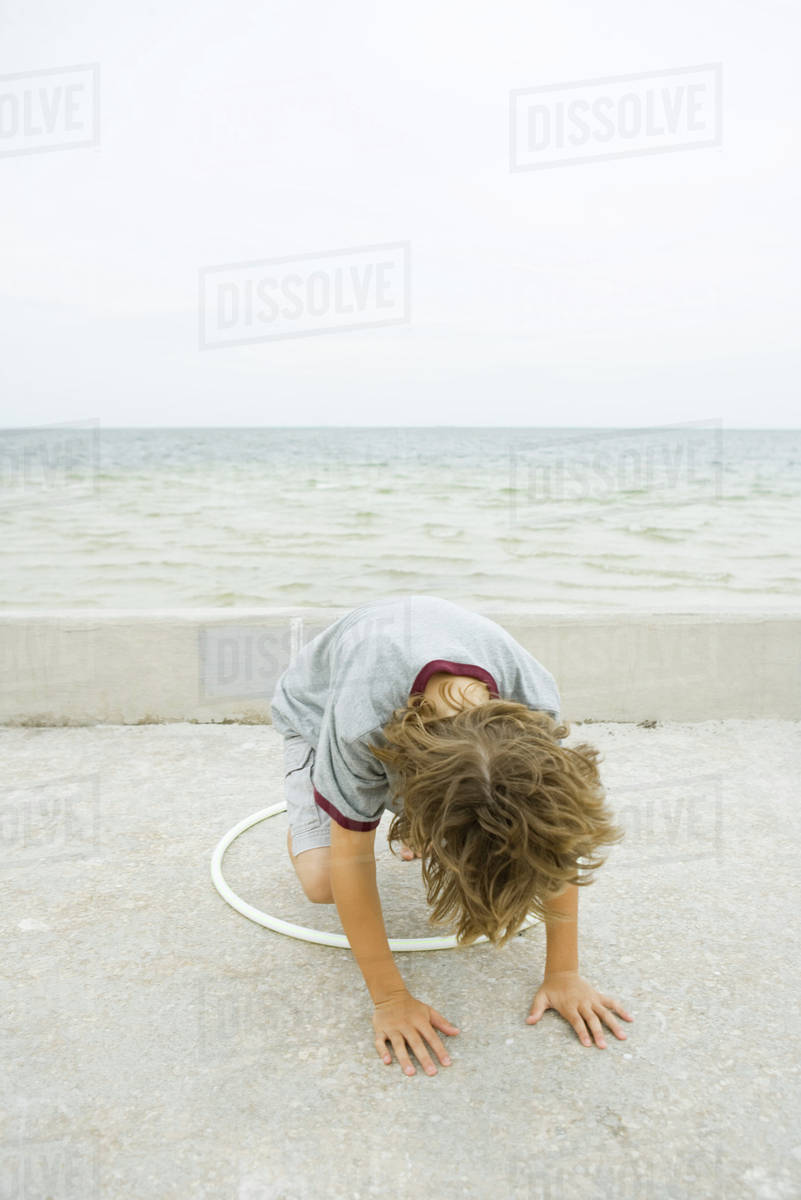 Boy crouching on all fours, playing with plastic hoop, head down ...